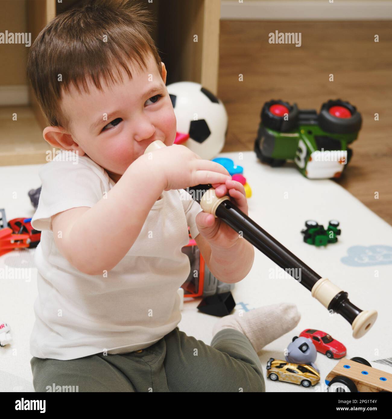 Toddler baby plays the flute sitting on the floor in the children's ...