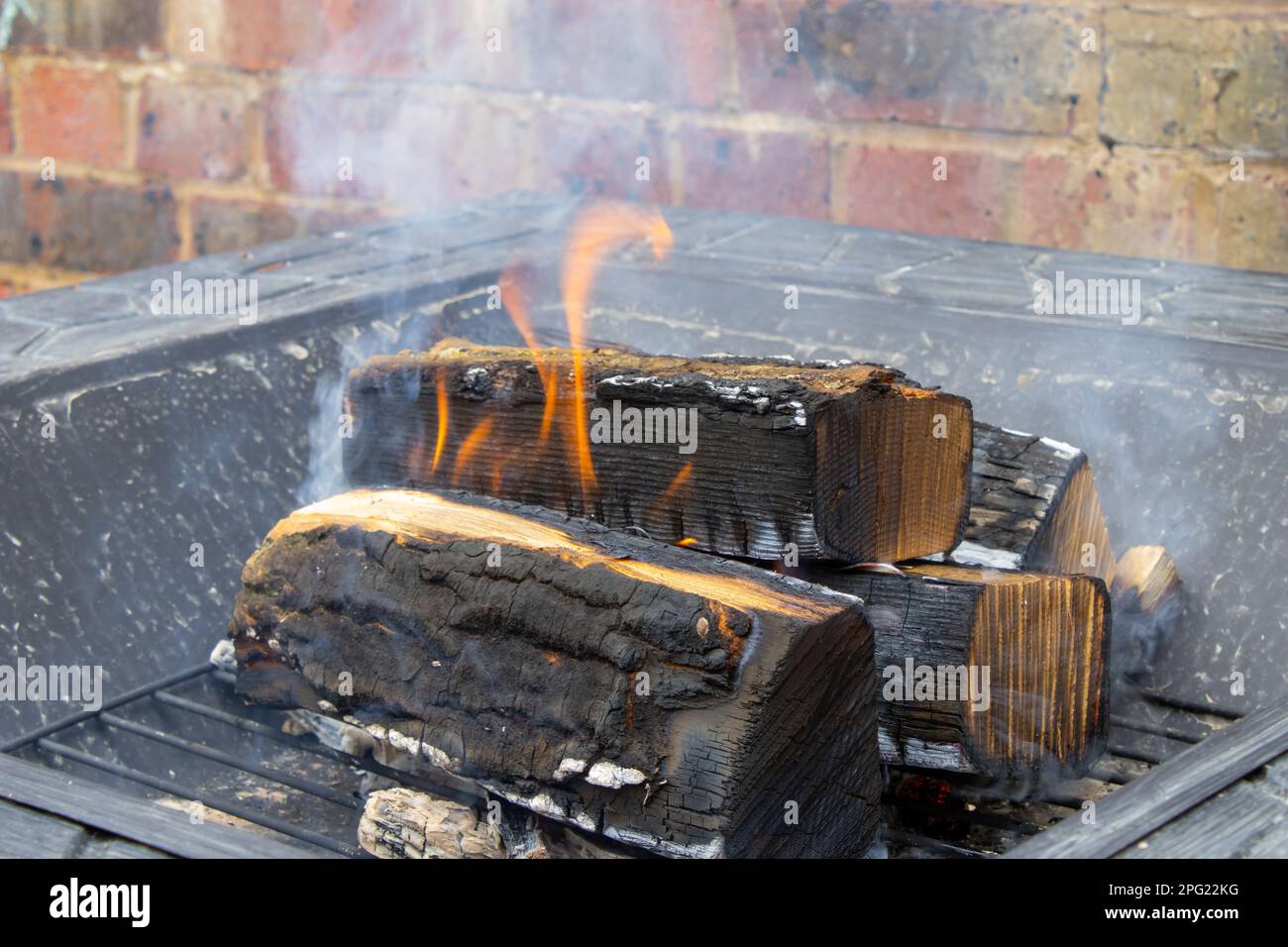 Logs burning in a black fire pit in front of a brick wall Stock Photo ...