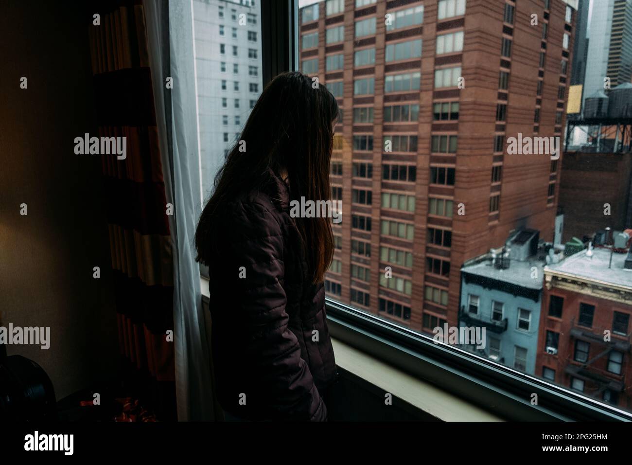 Woman looking at city out of window Stock Photo - Alamy