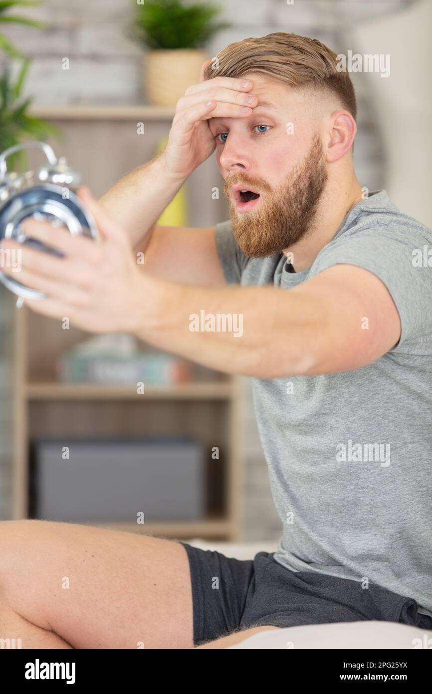 scared man at home looking at clock being late Stock Photo - Alamy
