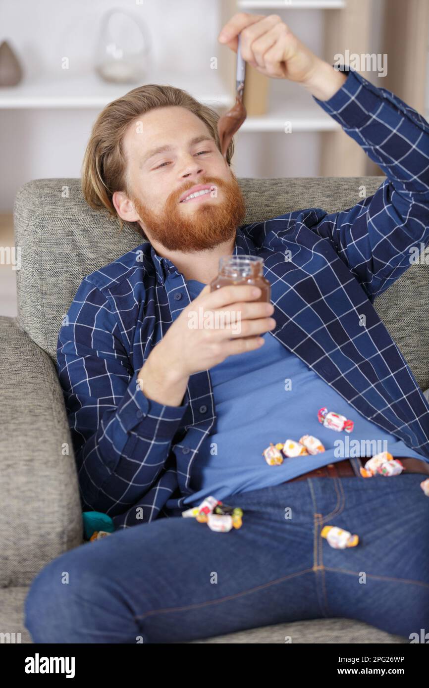 happy man eating chocolate and sweets on couch Stock Photo - Alamy