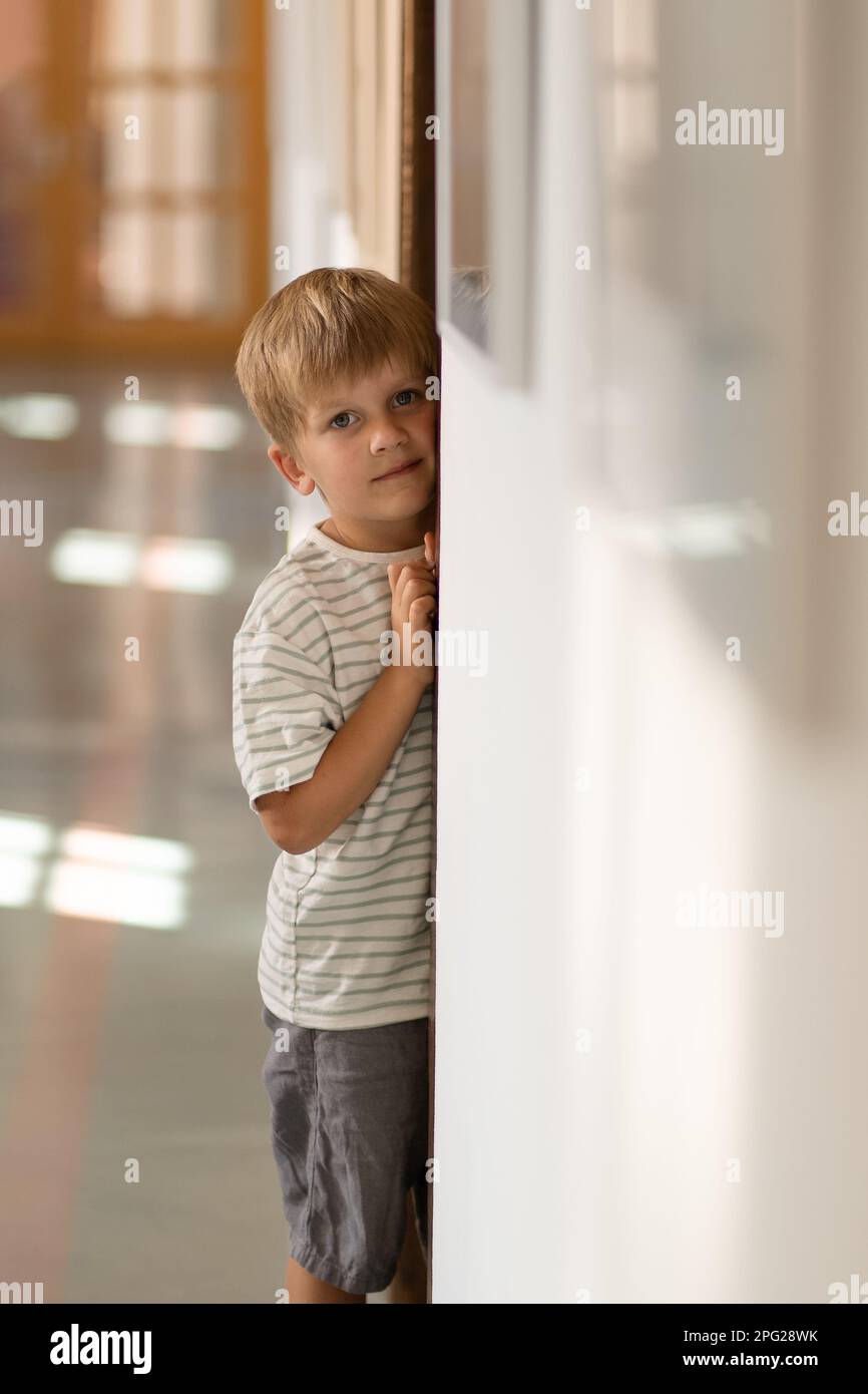 Boy playing hide and seek in corridor, Active kid looking out while ...