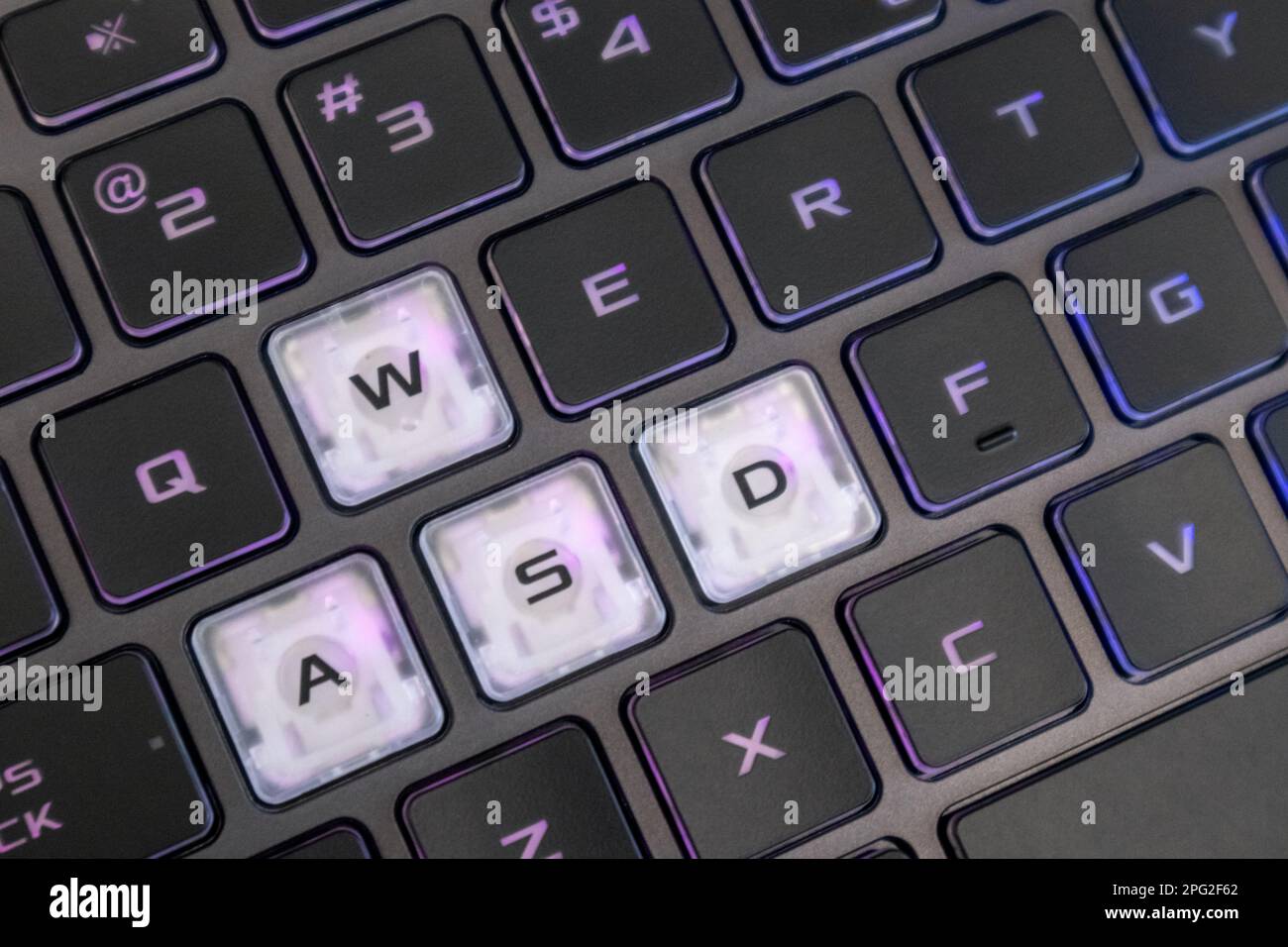 Highlighted gaming keys with purple gradient light. Powerful dark notebook keyboard close-up ...