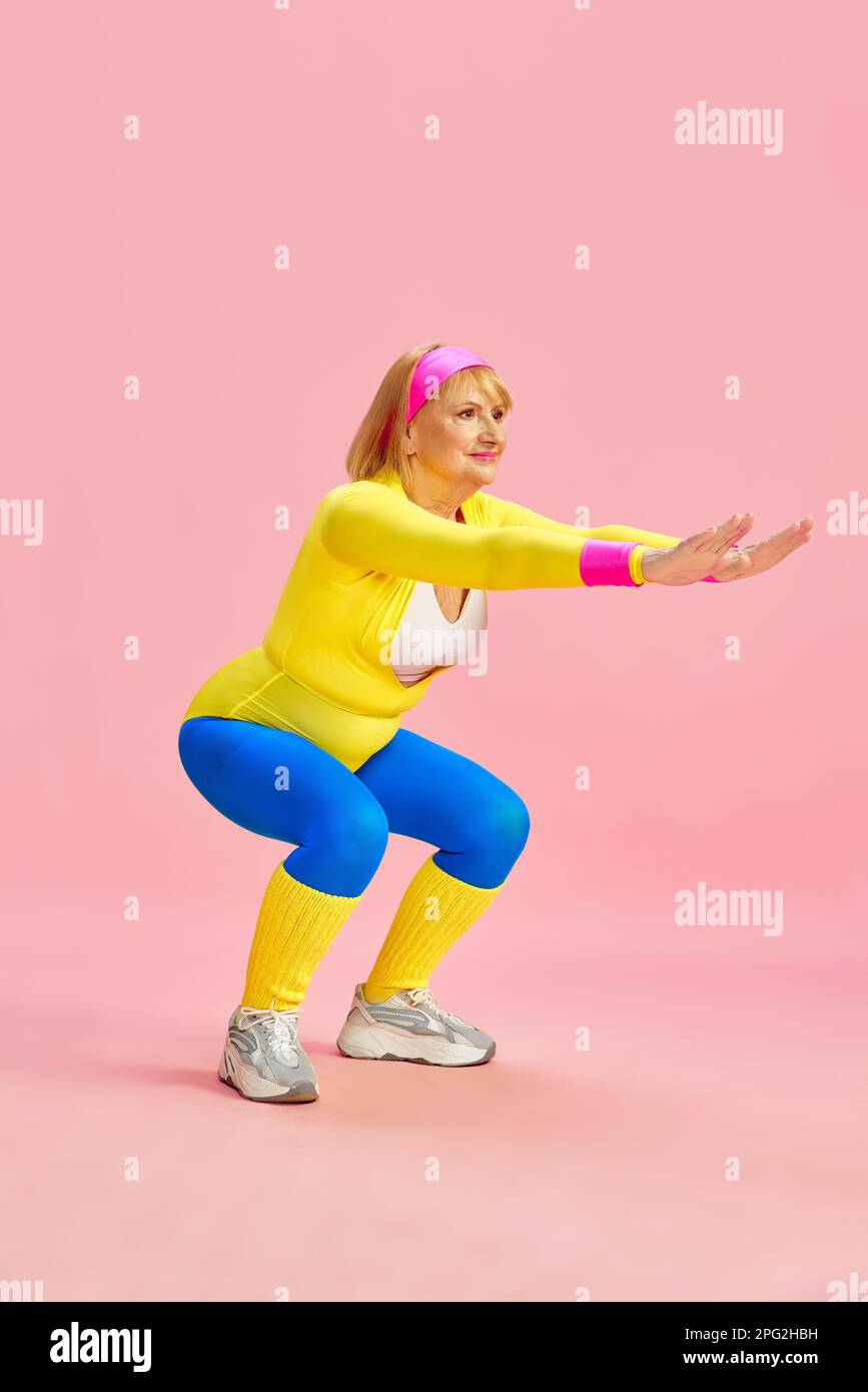 Elderly beautiful woman in colorful sportswear training, doing squats ...