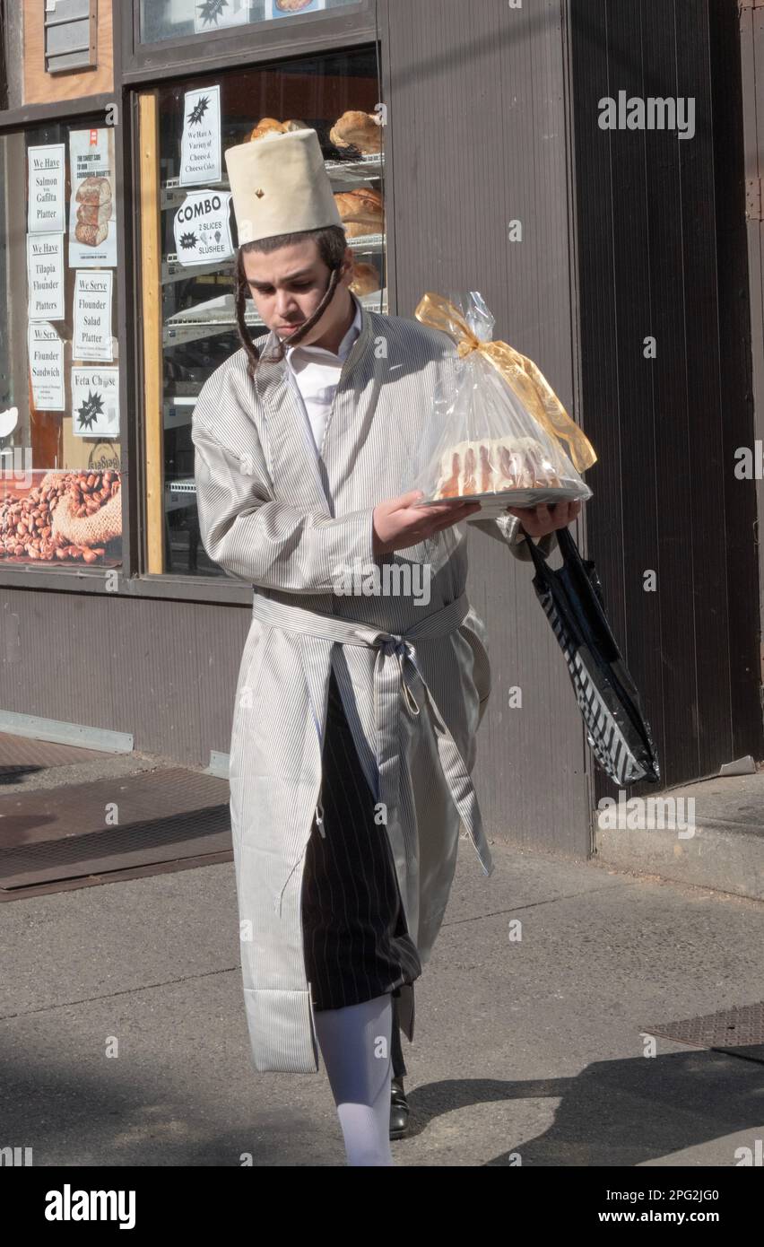 A young Hasidic boy in a costume & with long peyes brings a cake to ...