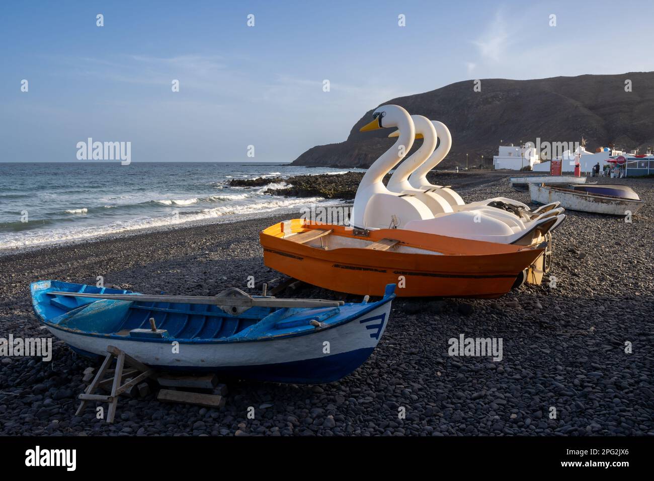 Pebble beach in the winter season. Fishing wooden boats and swans water ...