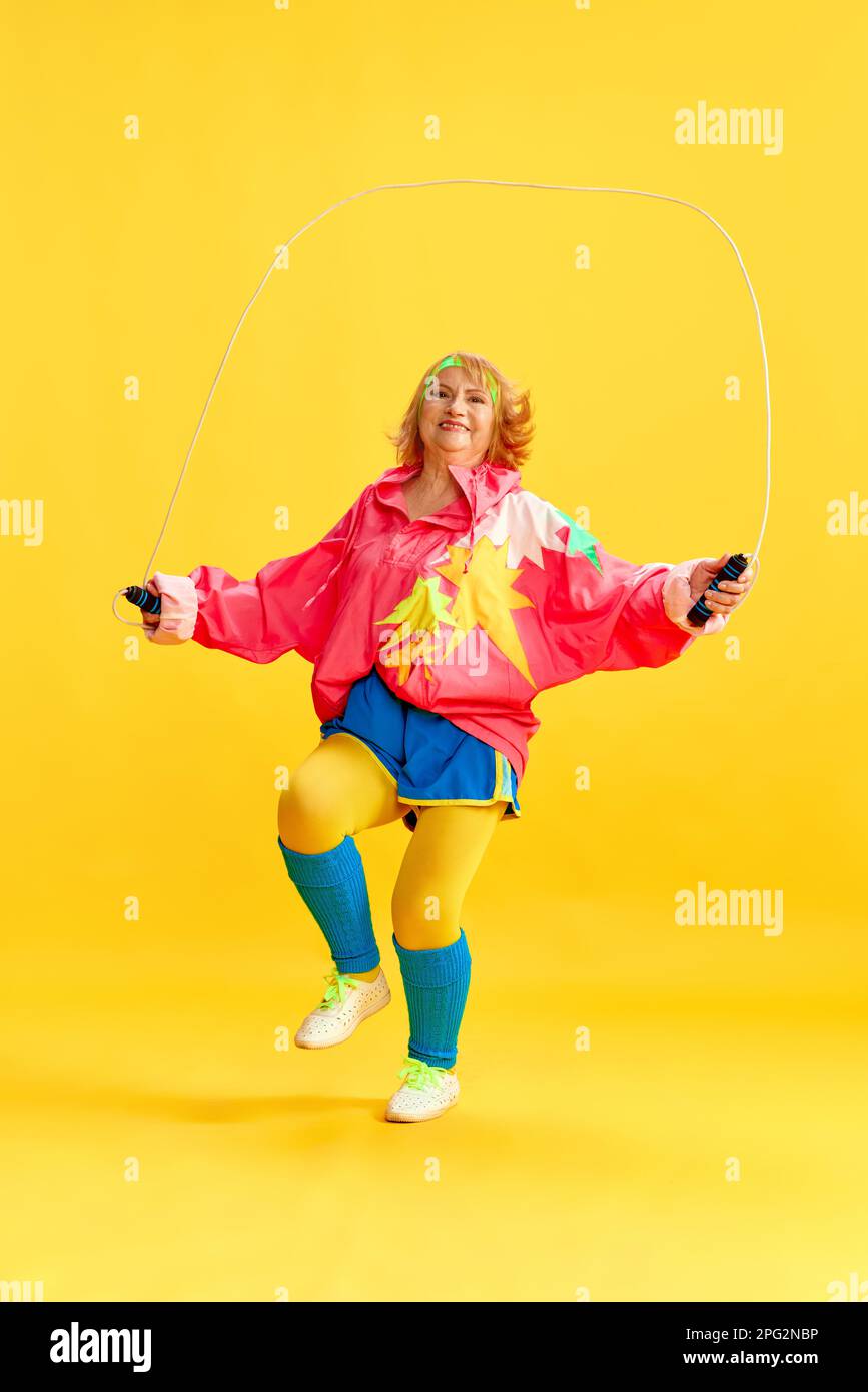 Happy senior sportive woman in colorful uniform training, jumping rope ...