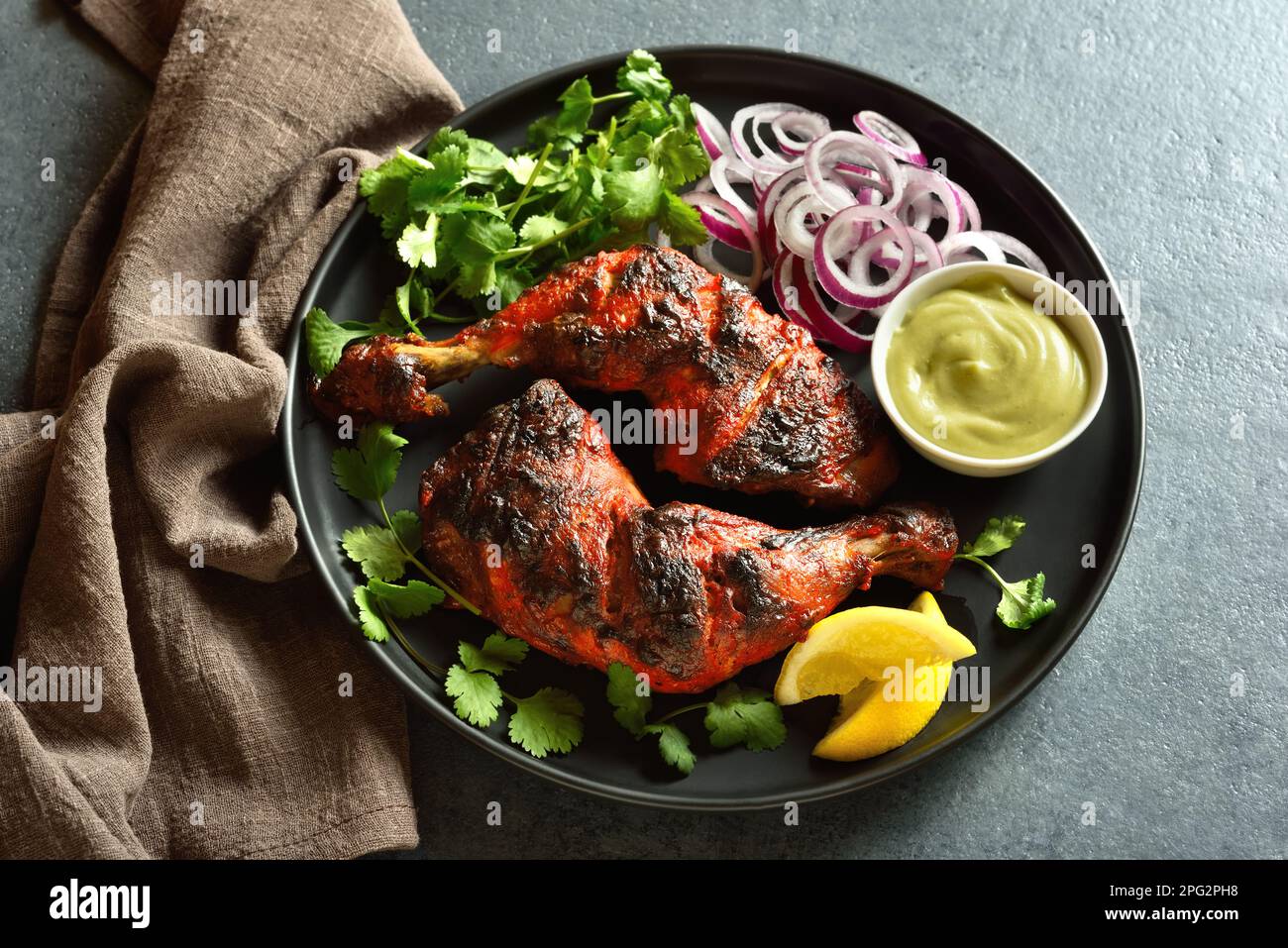 Tandoori chicken served with cilantro and onion on plate over dark ...