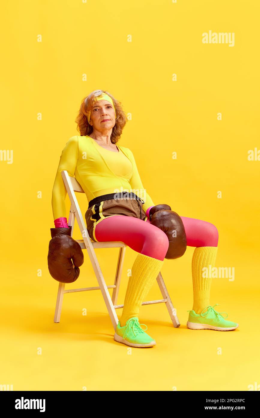Elderly sportive woman in colorful uniform sitting on chair in retro ...