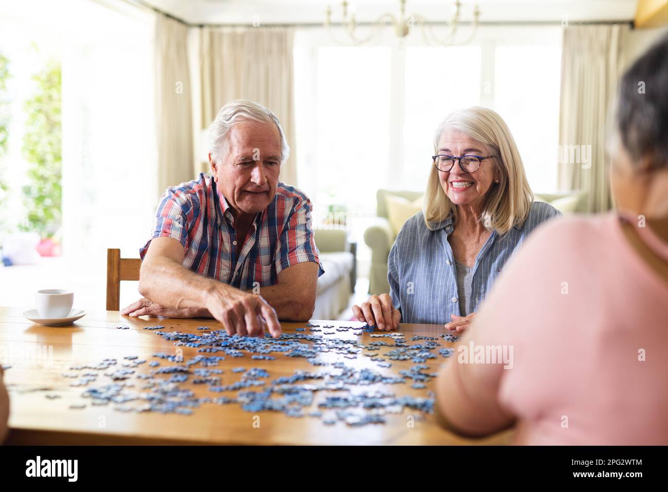 Happy group of diverse senior friends sitting at table doing jigsaw ...
