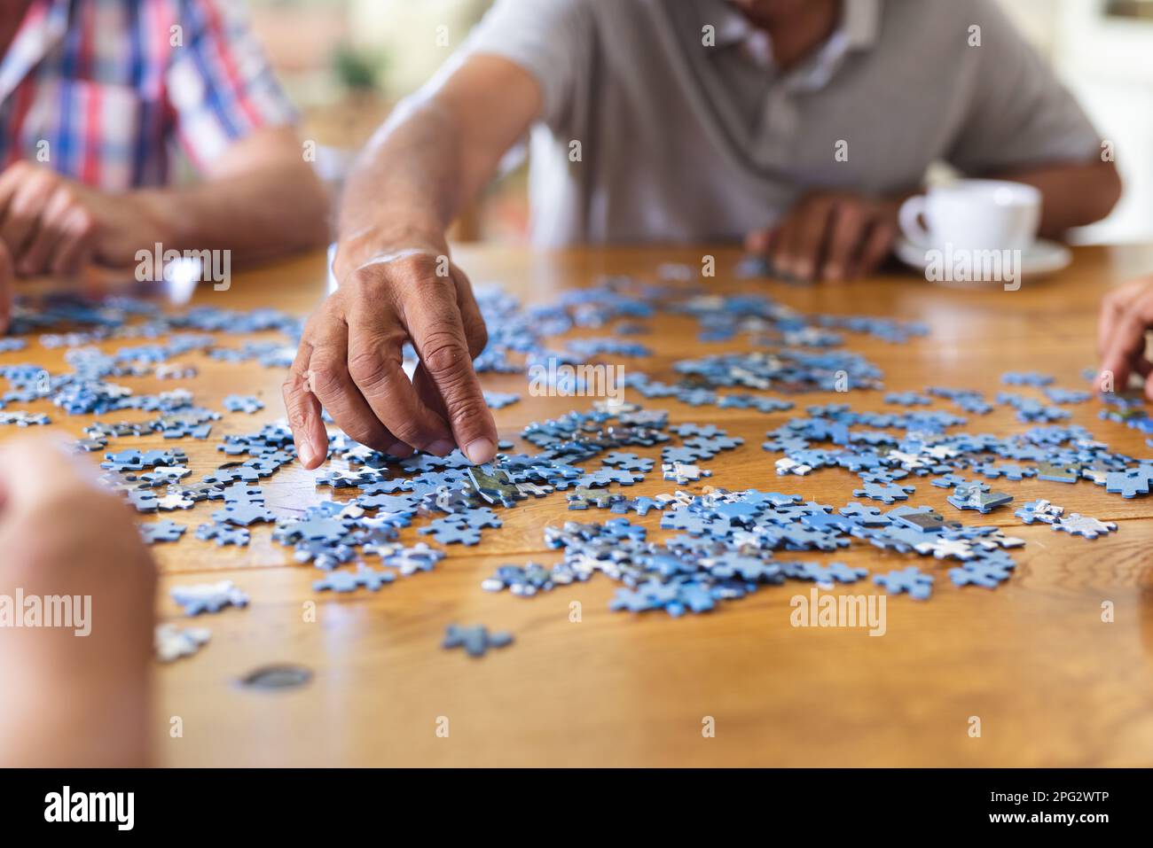 Hands of diverse senior friends sitting at table doing jigsaw puzzle ...