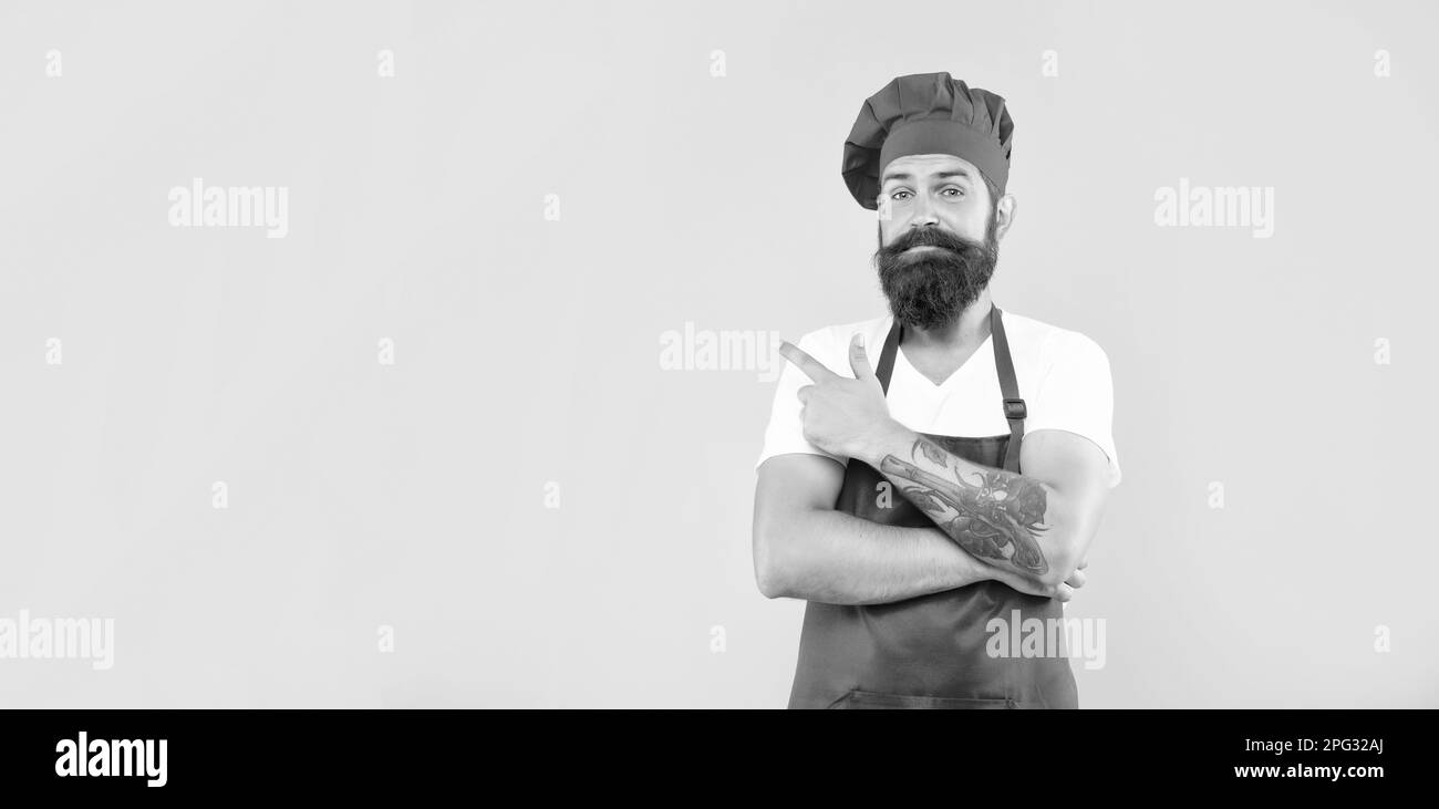 Man cook in toque and apron pointing finger aside yellow background ...