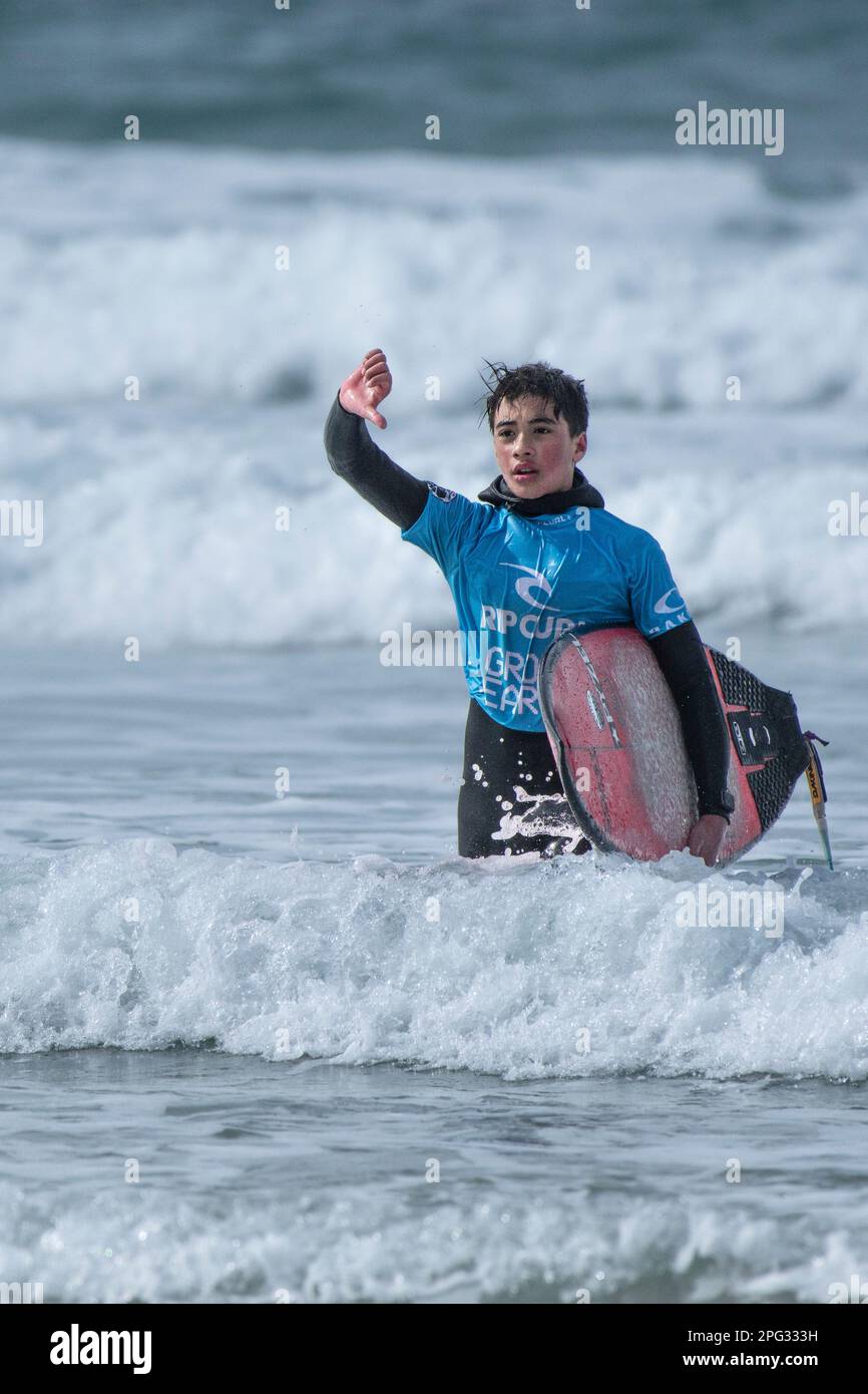 A young male surfer carrying his surfboard giving a thumbs down and ...