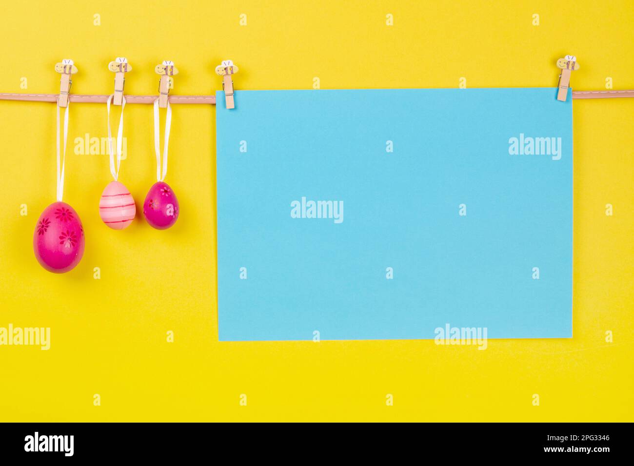 Blank blue sheet of paper and three pink Easter eggs hang at rope on ...
