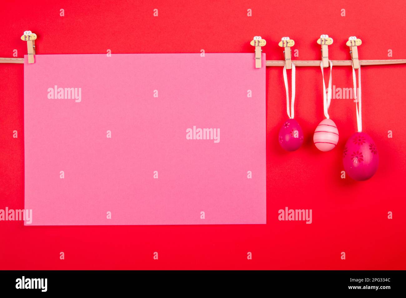Blank rose colored sheet of paper and three pink Easter eggs hang at ...