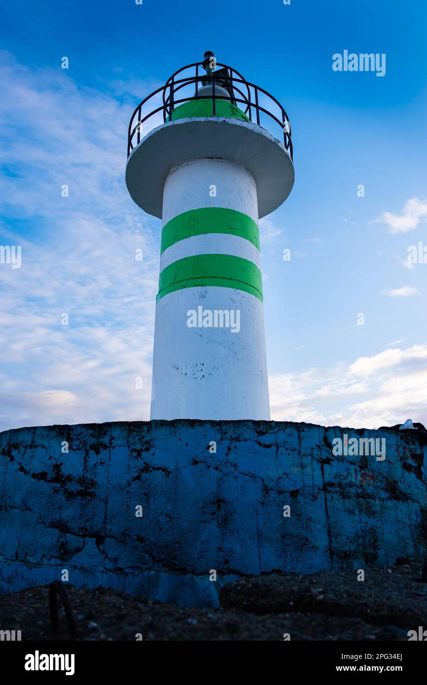 A vertical low angle shot of a green white lighthouse in a bright blue ...