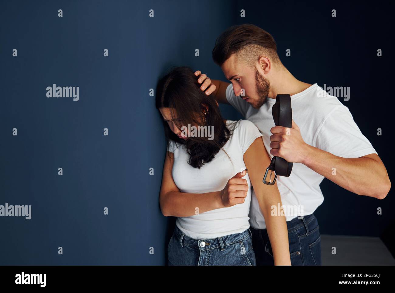 Near blue wall. Violent aggressive young man with belt threatening his ...