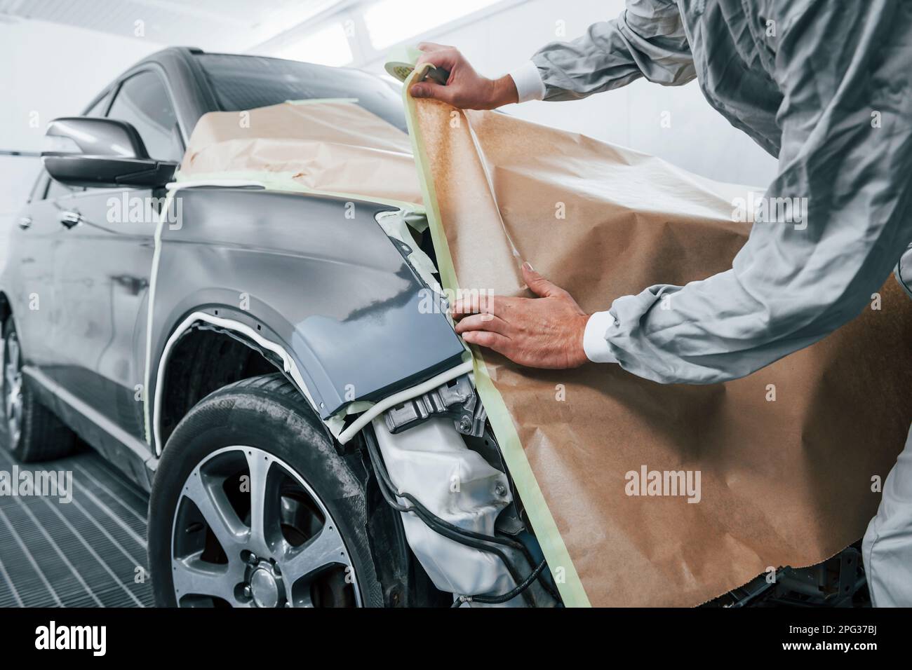 Covering car by brown cloth. Caucasian automobile repairman in uniform ...