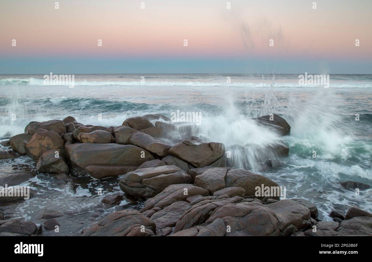 Coastal scene showing a wave crashing on rocks with a large wave breaking in the distance Stock ...