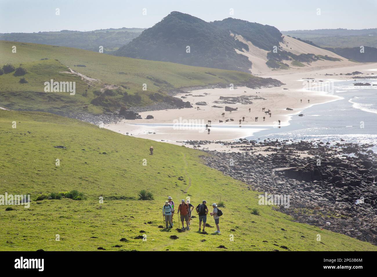 Scenic view of hikers walking up a grassy slope against the backdrop of ...