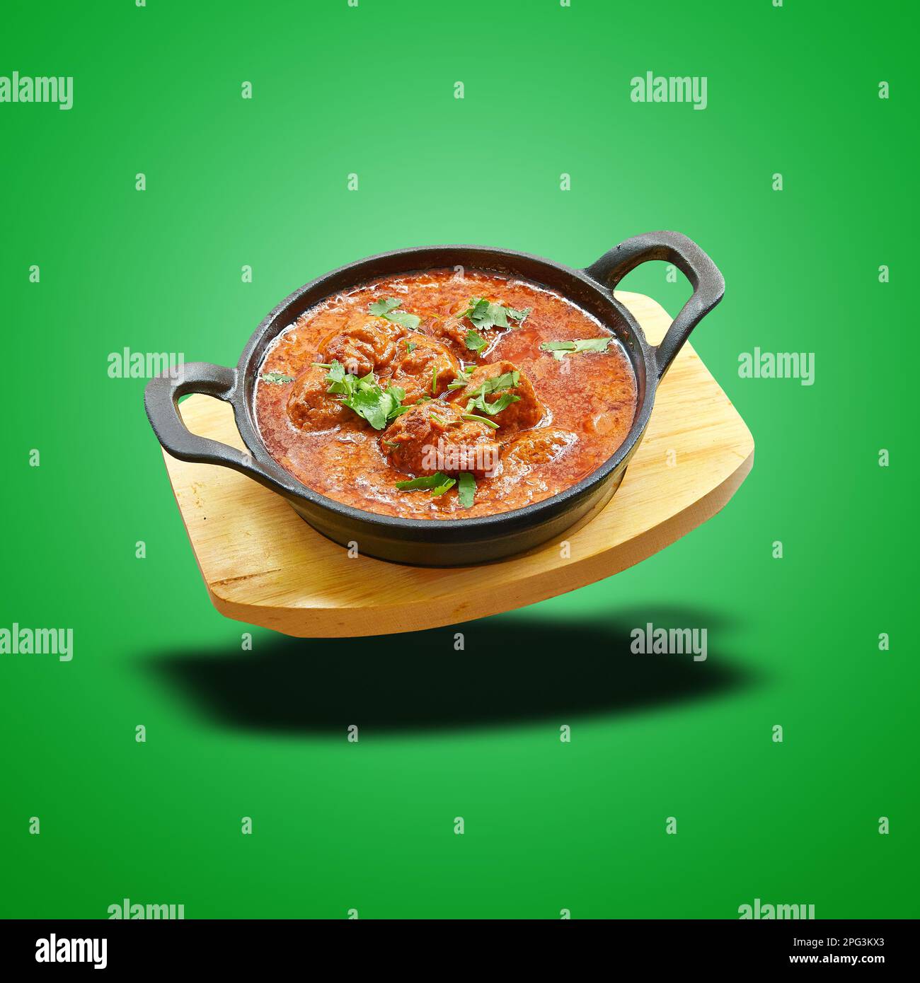 Floating Chicken tikka masala baked in little pan on green gradient ...
