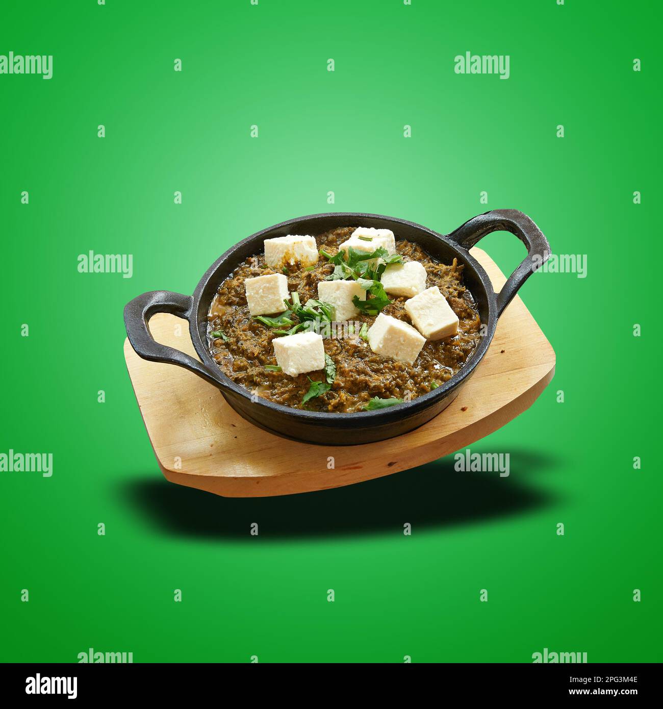 Floating Palak paneer baked in little pan on green gradient background ...