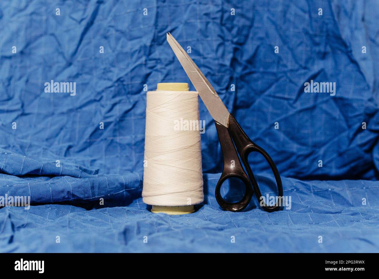 A white spool of thread arranged neatly next to scissors on a flat ...