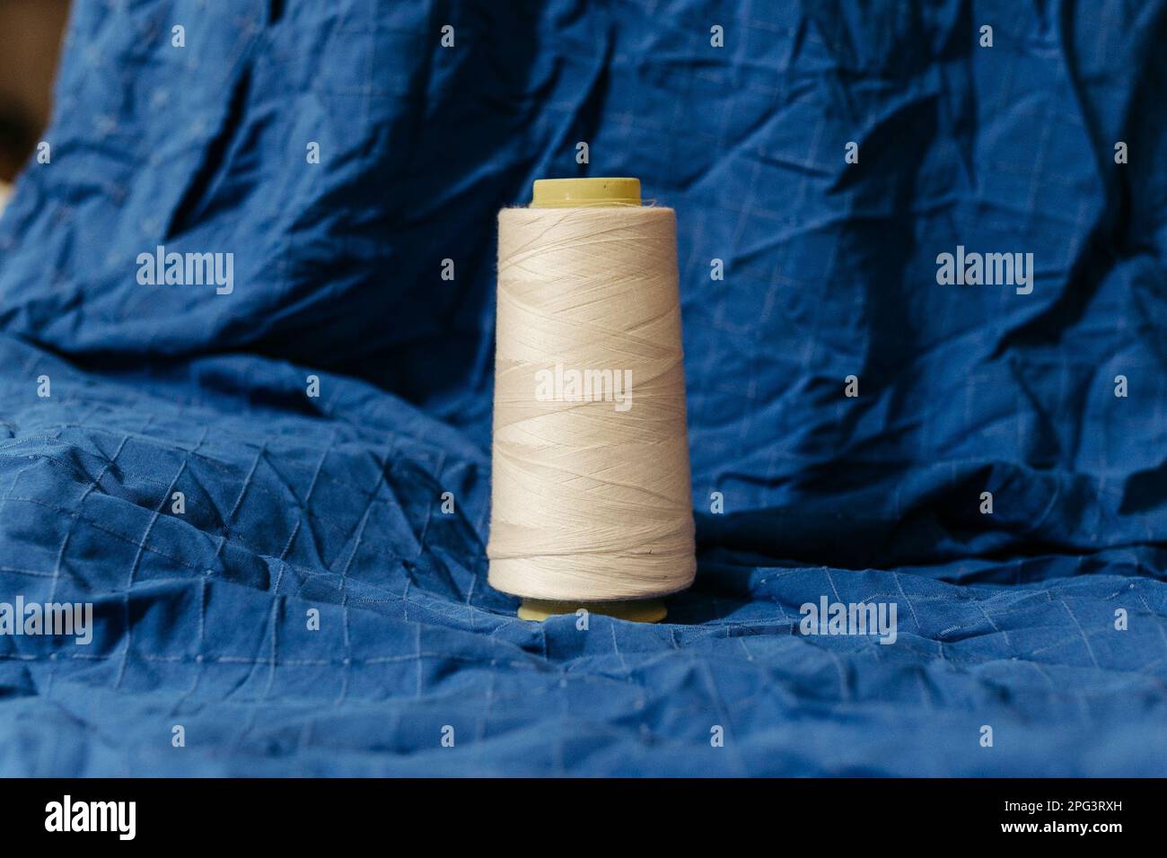 A white spool of thread arranged neatly on a flat surface, with blue ...