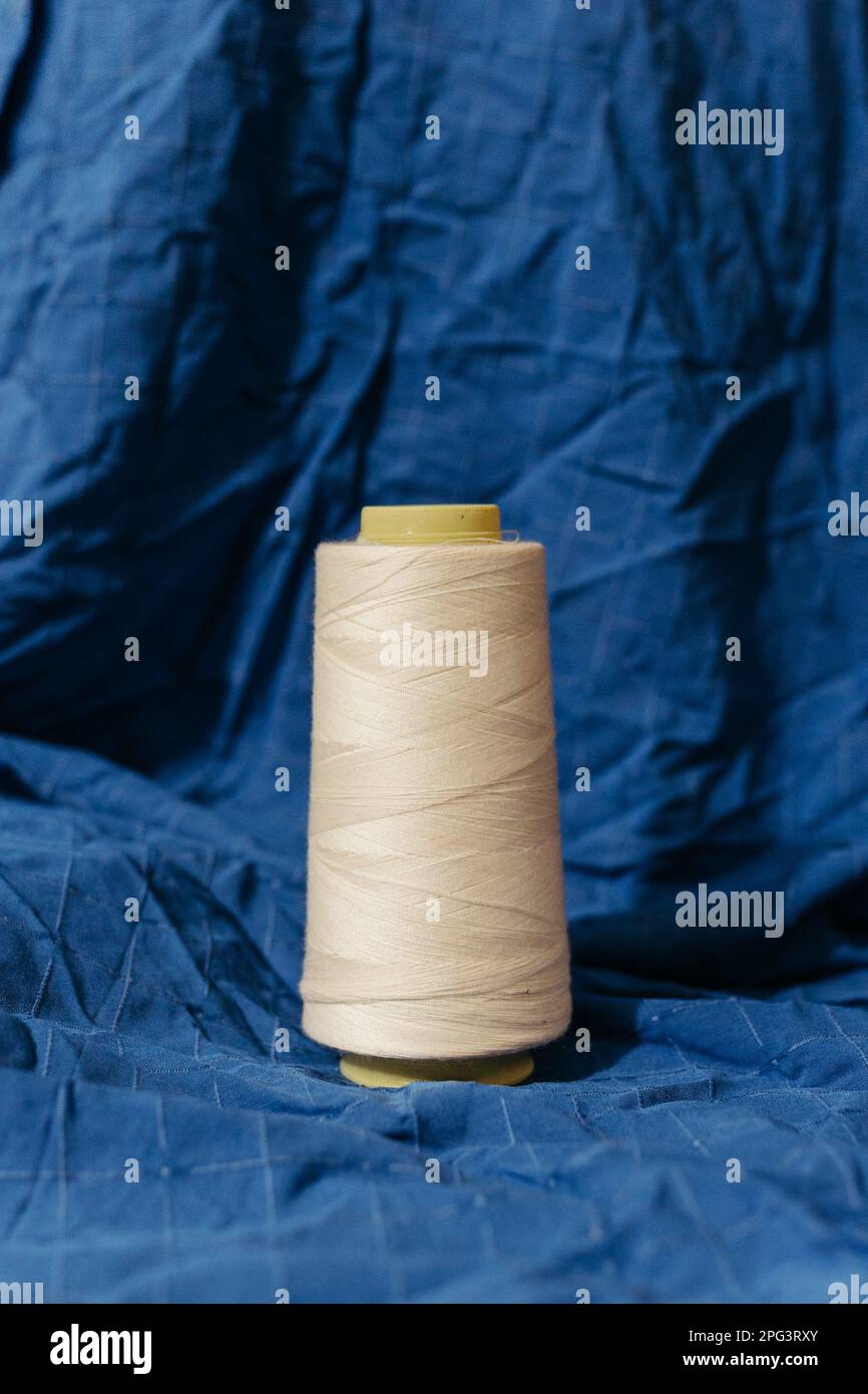 A white spool of thread arranged neatly on a flat surface, with blue ...