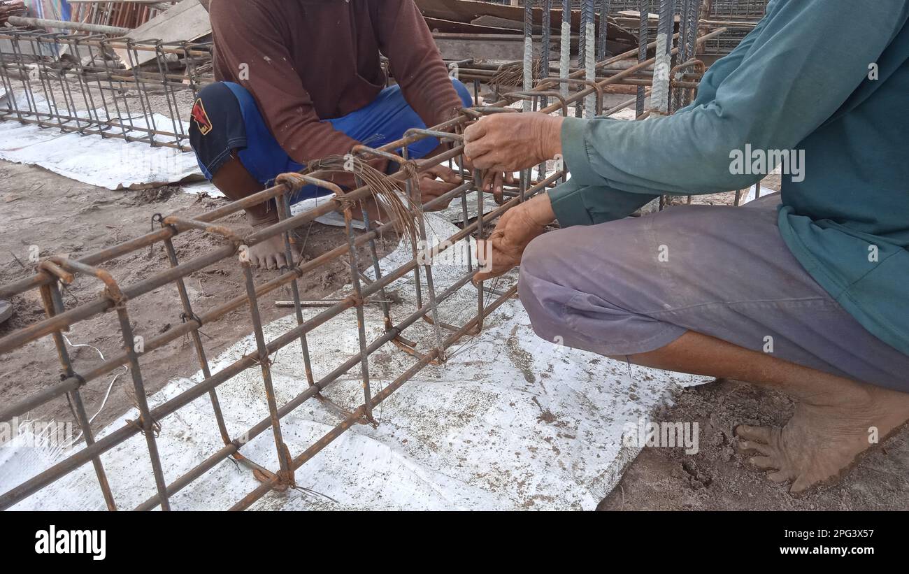 Worker's hands stringing iron rods with wire for beam section at ...