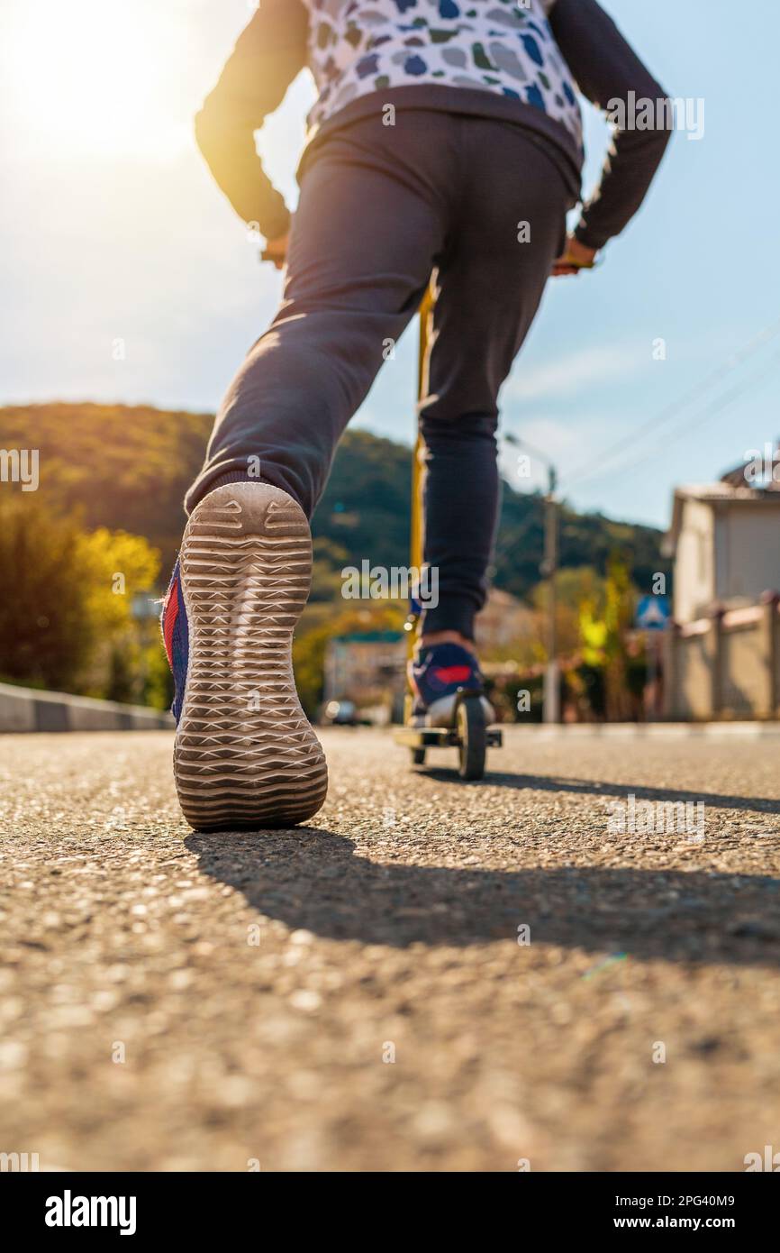 A teenage boy rides a scooter, pushing off with his left foot. Legs ...
