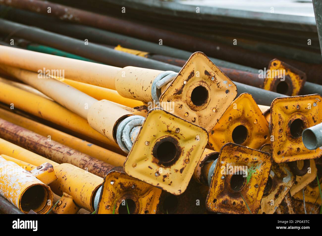Old scaffold tubes are stored outside in a pile. Different yellow tubes ...