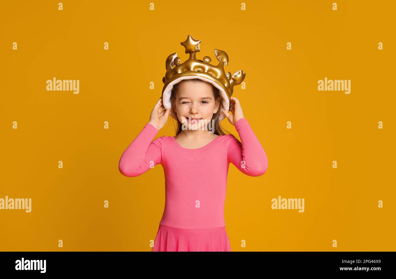 Cute girl in inflatable crown on yellow background. Little princess ...