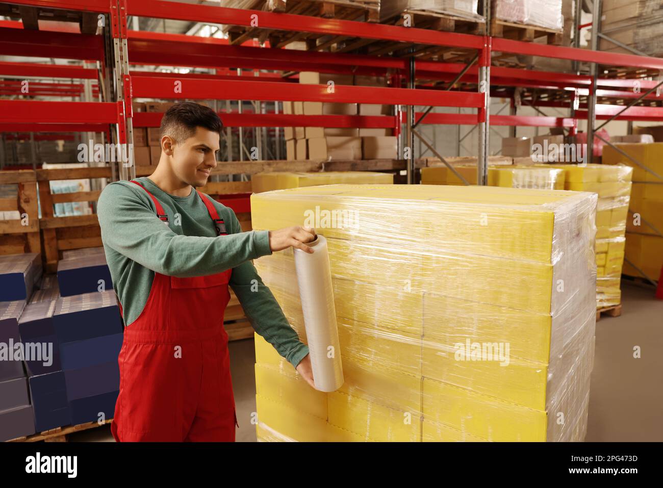 Worker wrapping boxes in stretch film at warehouse Stock Photo - Alamy