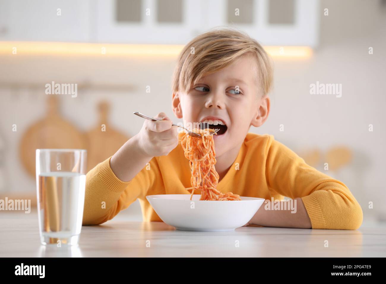 Happy boy eating tasty pasta at table in kitchen Stock Photo - Alamy