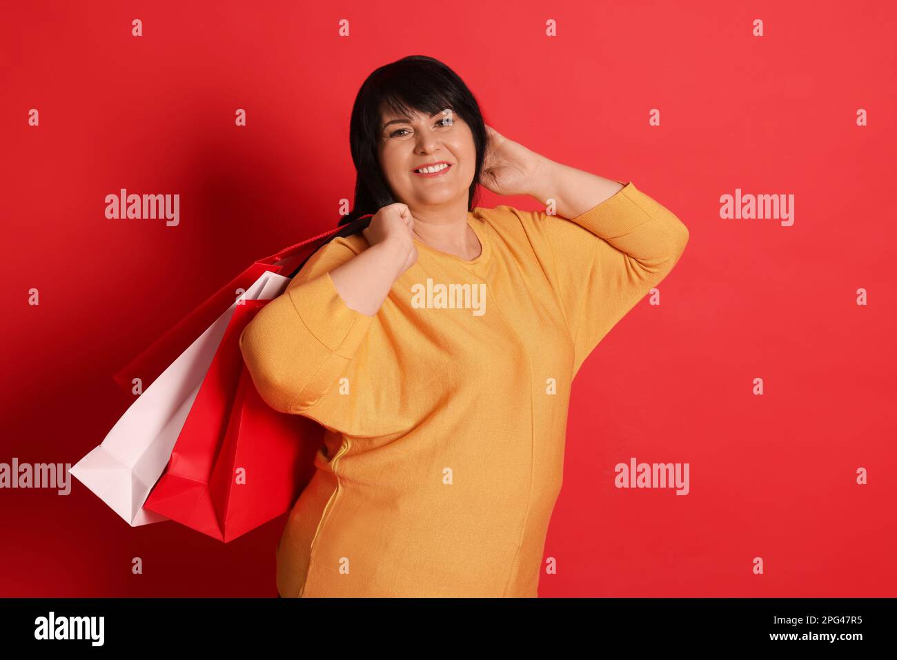 Beautiful overweight mature woman with shopping bags on red background ...