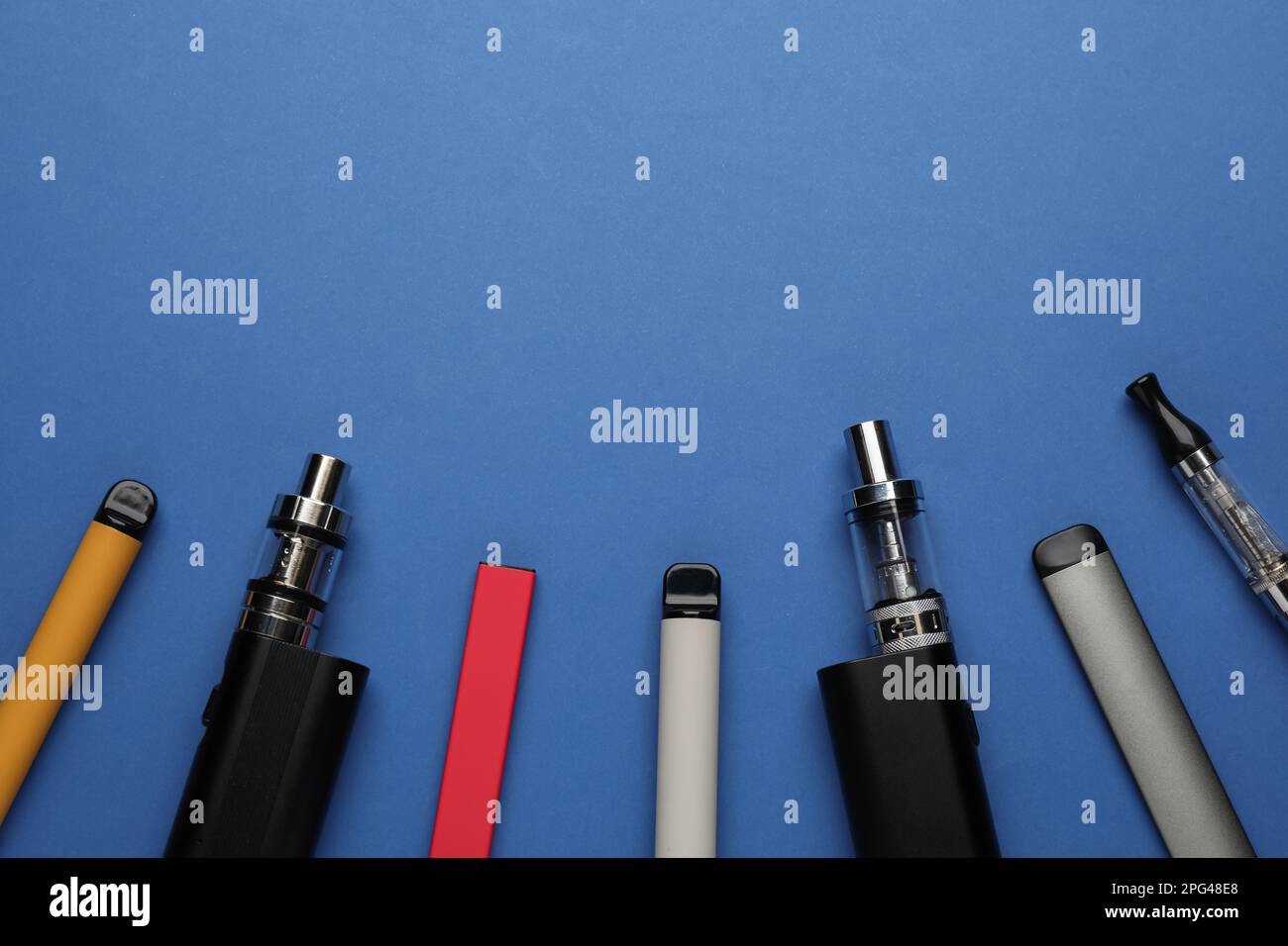 Many electronic smoking devices on blue background, flat lay. Space for ...