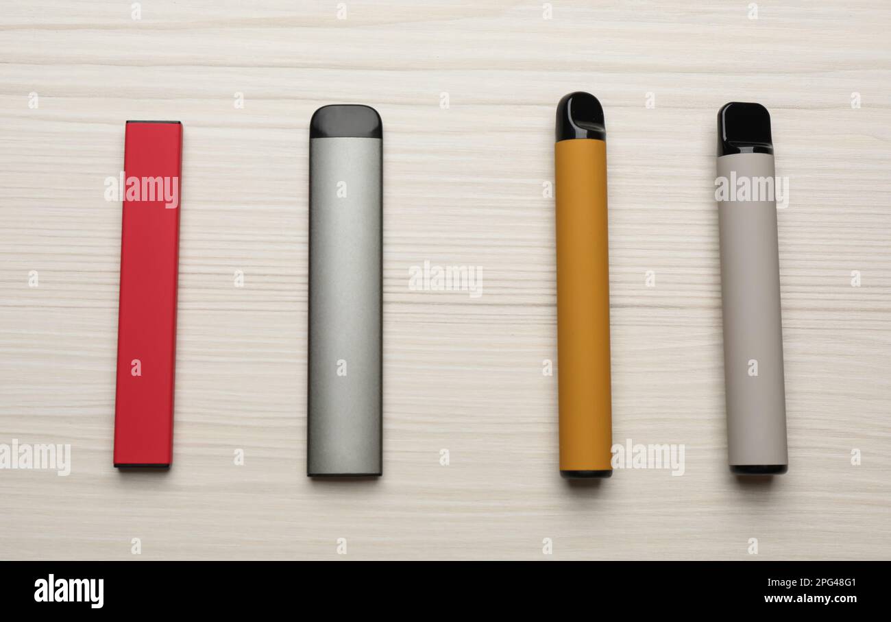 Different disposable electronic cigarettes on white wooden table, flat ...