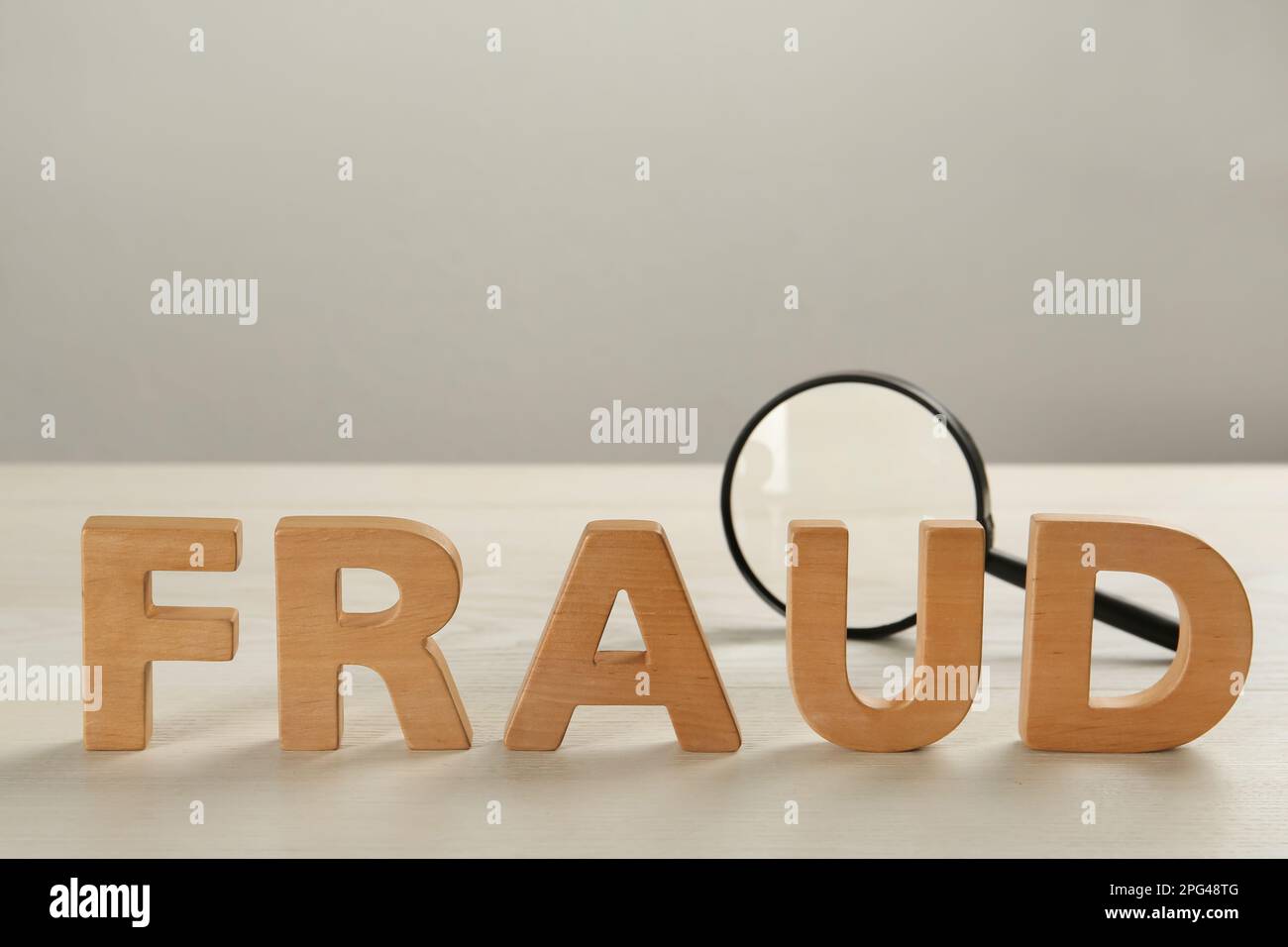Word Fraud made of wooden letters and magnifying glass on white table ...