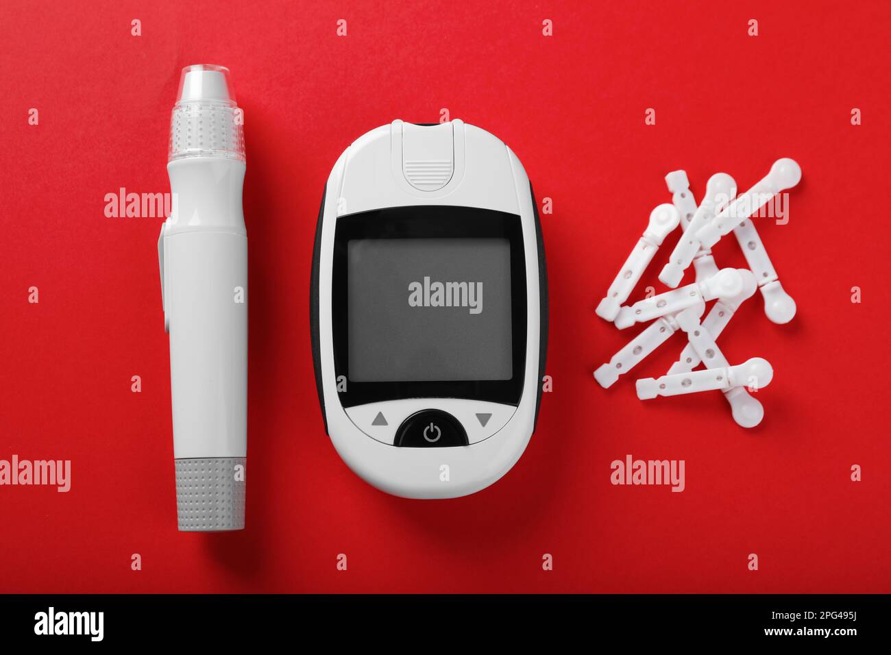 Digital glucometer, lancets and pen on red background, flat lay ...