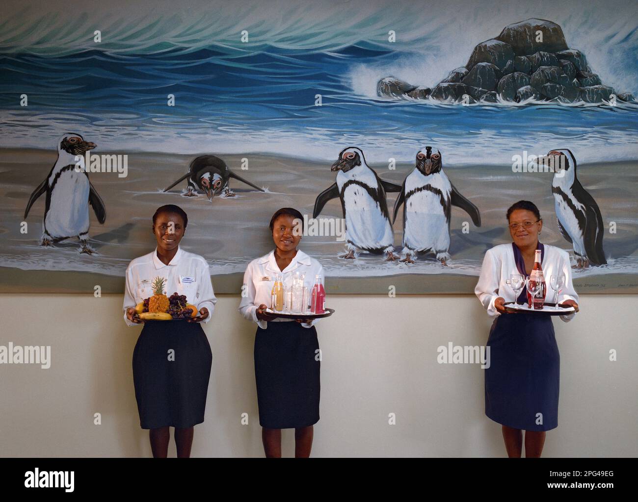 Three waitresses stand with drinks in front of a painting in the lounge ...