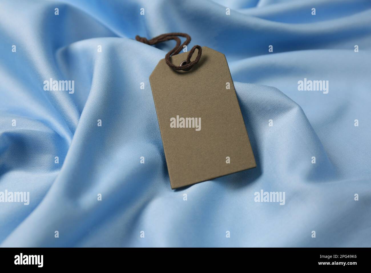 Blank grey tag on light blue silky fabric, closeup. Space for text ...