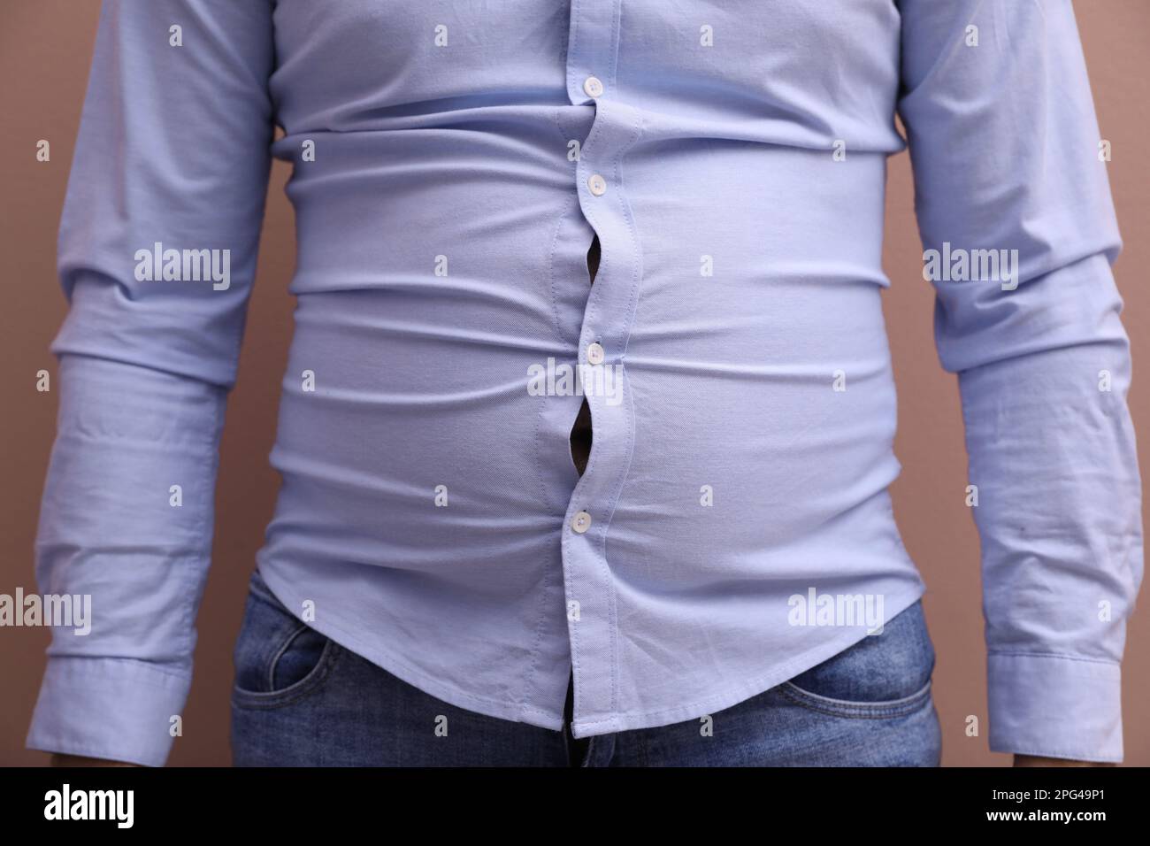 Man wearing tight shirt on pale pink background, closeup. Overweight ...