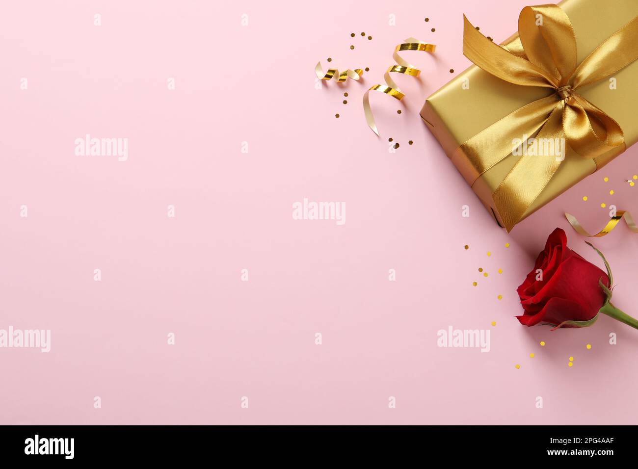 Golden gift box, red rose, confetti and streamers on pink background ...