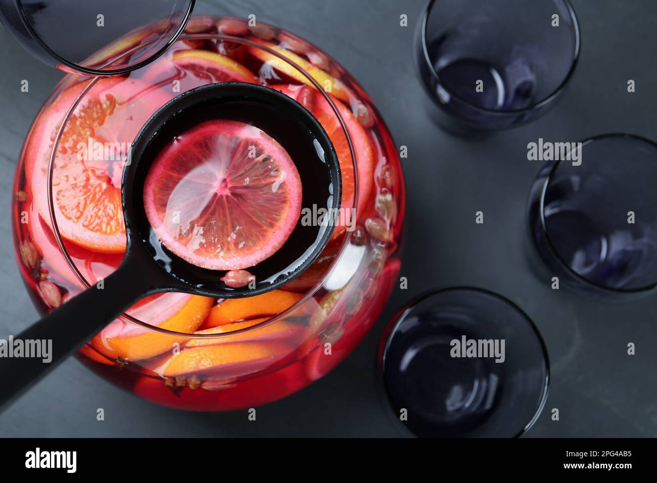 Ladle with aromatic punch drink above glass bowl on black table, top ...