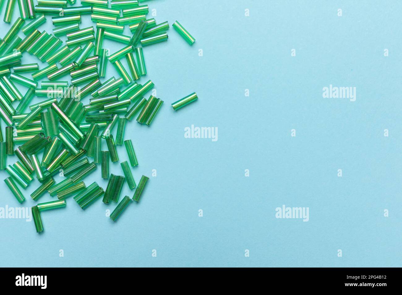Pile of green bugle beads on light blue background, flat lay. Space for ...