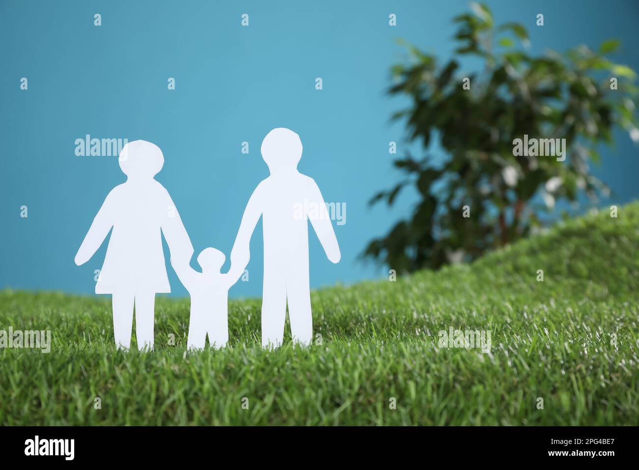 Paper cutout of parents with their child on green grass against light ...
