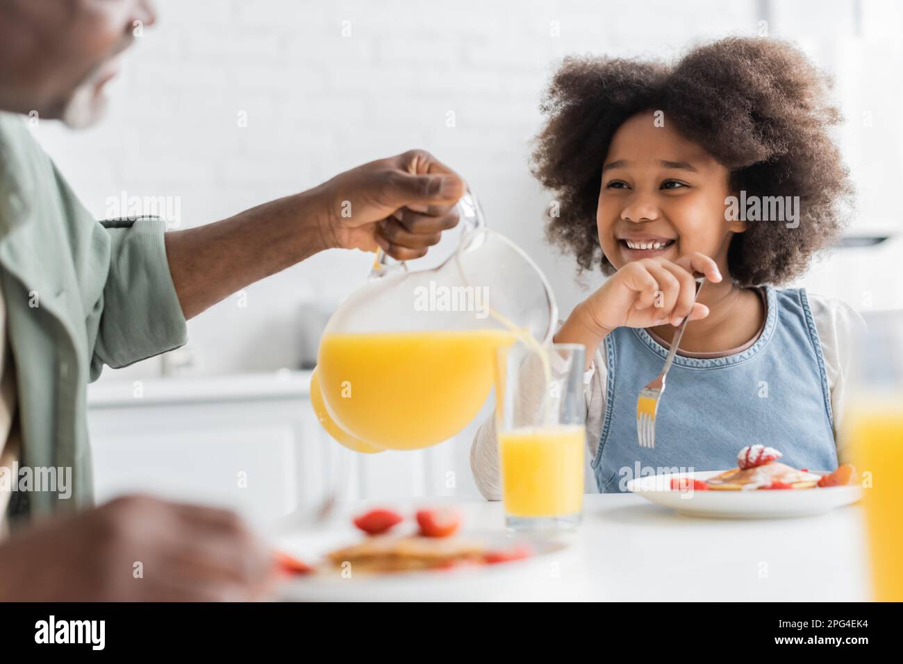 happy african american girl looking at grandfather pouring orange juice during breakfast,stock ...