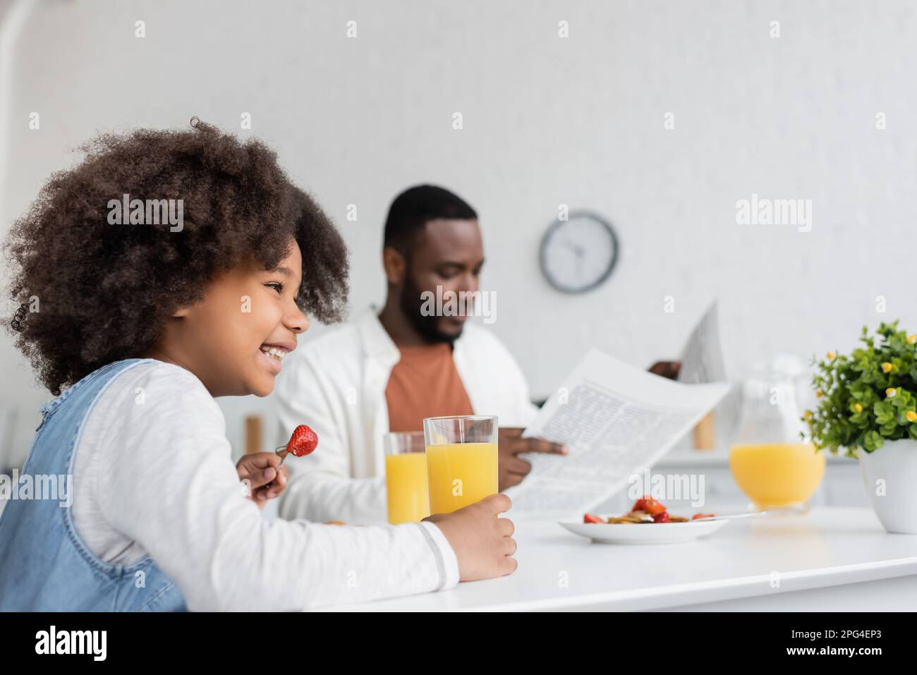 happy african american girl having breakfast while father reading newspaper on blurred ...