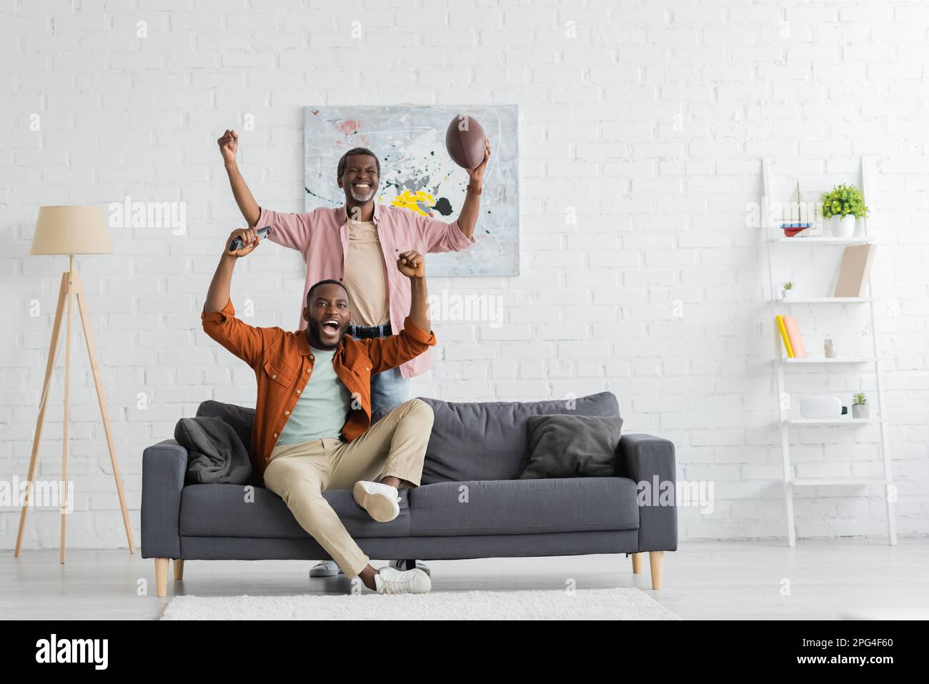 Excited african american father and son watching rugby match in modern ...
